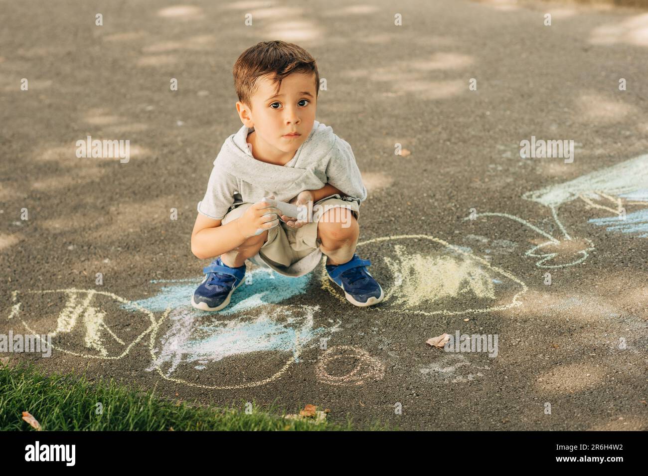 Adorable little boy drawing with a chalk outdoors. Outside activities ...