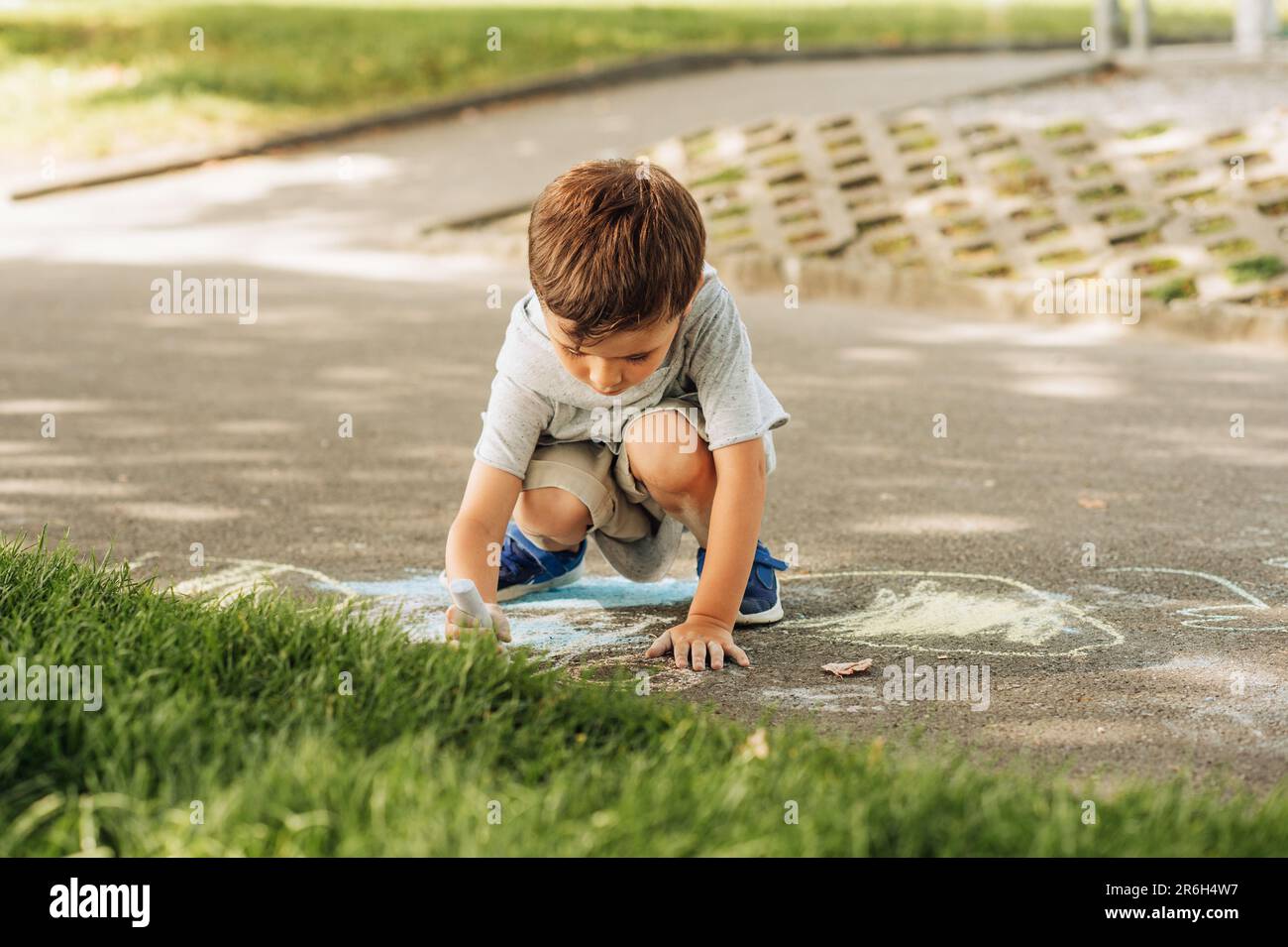Adorable little boy drawing with a chalk outdoors. Outside activities ...