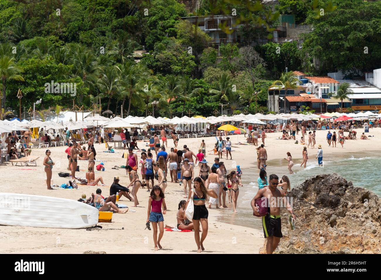 A cheerful crowd of people walking along a sandy beach shore, the ...