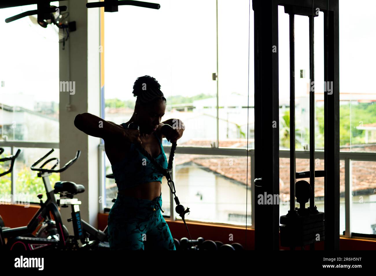 A young woman in a gym working out on a pull-up machine and kettlebell ...
