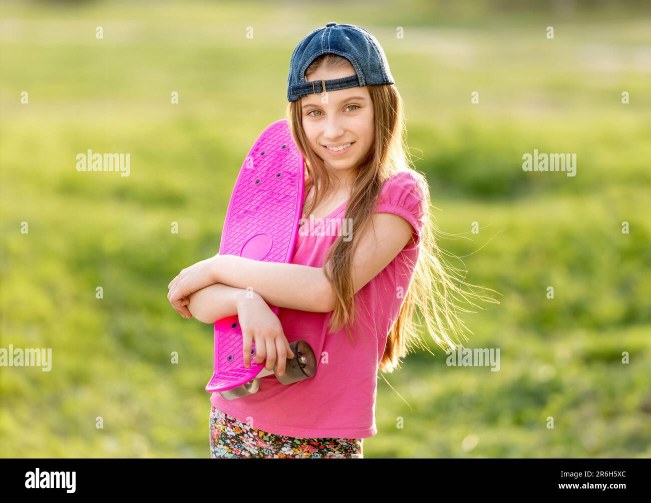 Attractive teenage girl with a cap on holding her bright pink skating ...