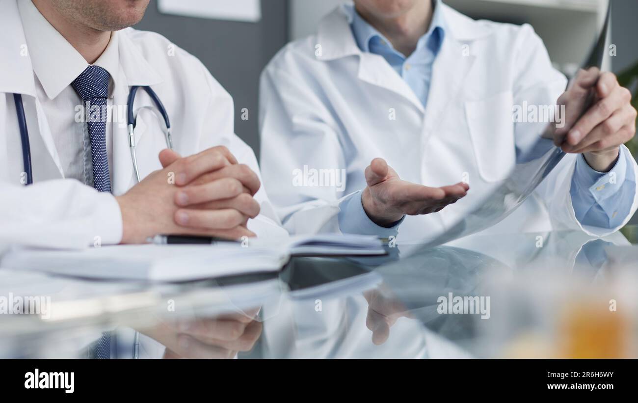 Two doctors look at x-rays and discuss the diagnosis. They sit a Stock ...