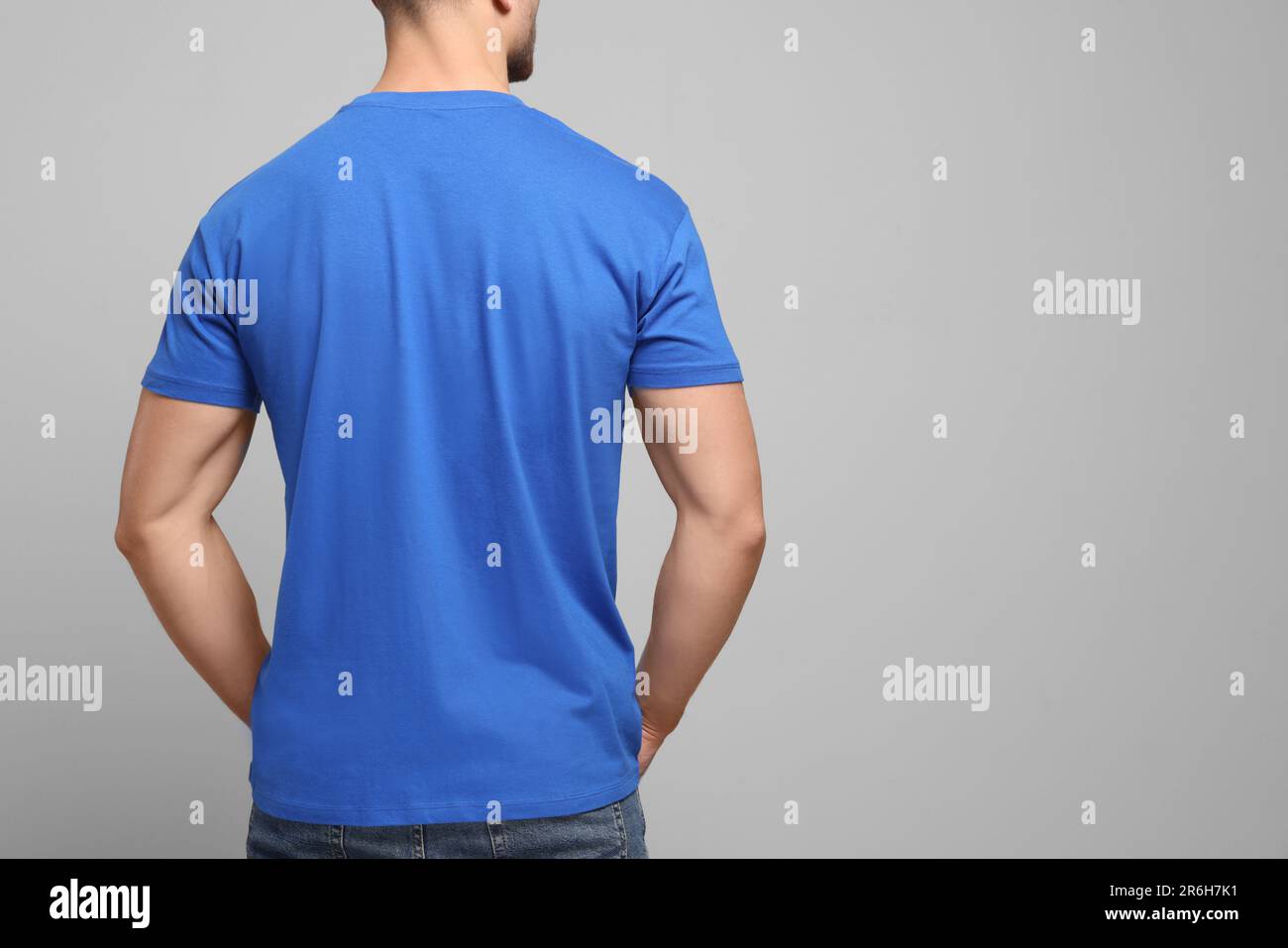 Man wearing blue t-shirt on light grey background, back view. Mockup ...