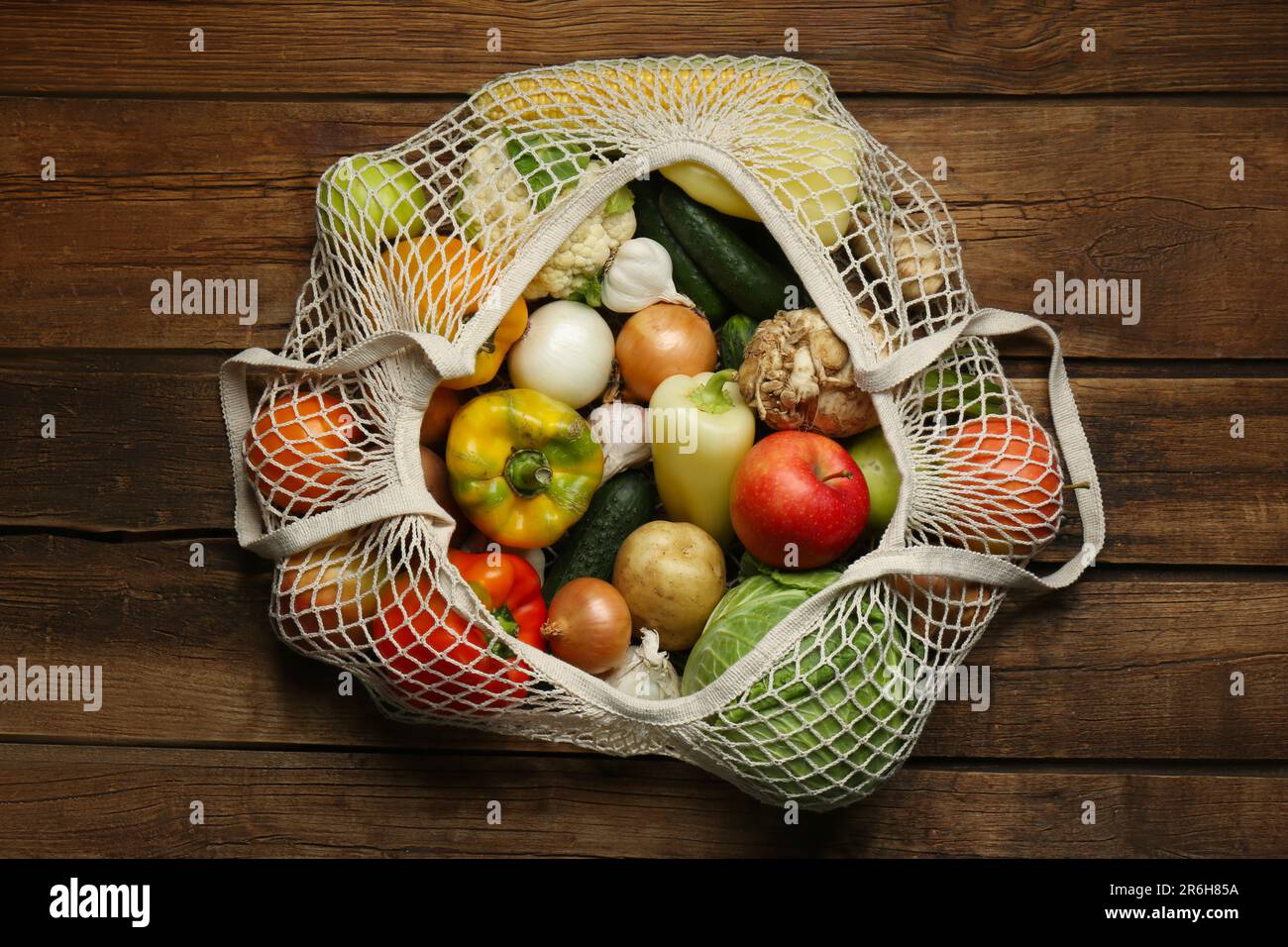 Different fresh vegetables in net bag on wooden table, top view. Farmer ...