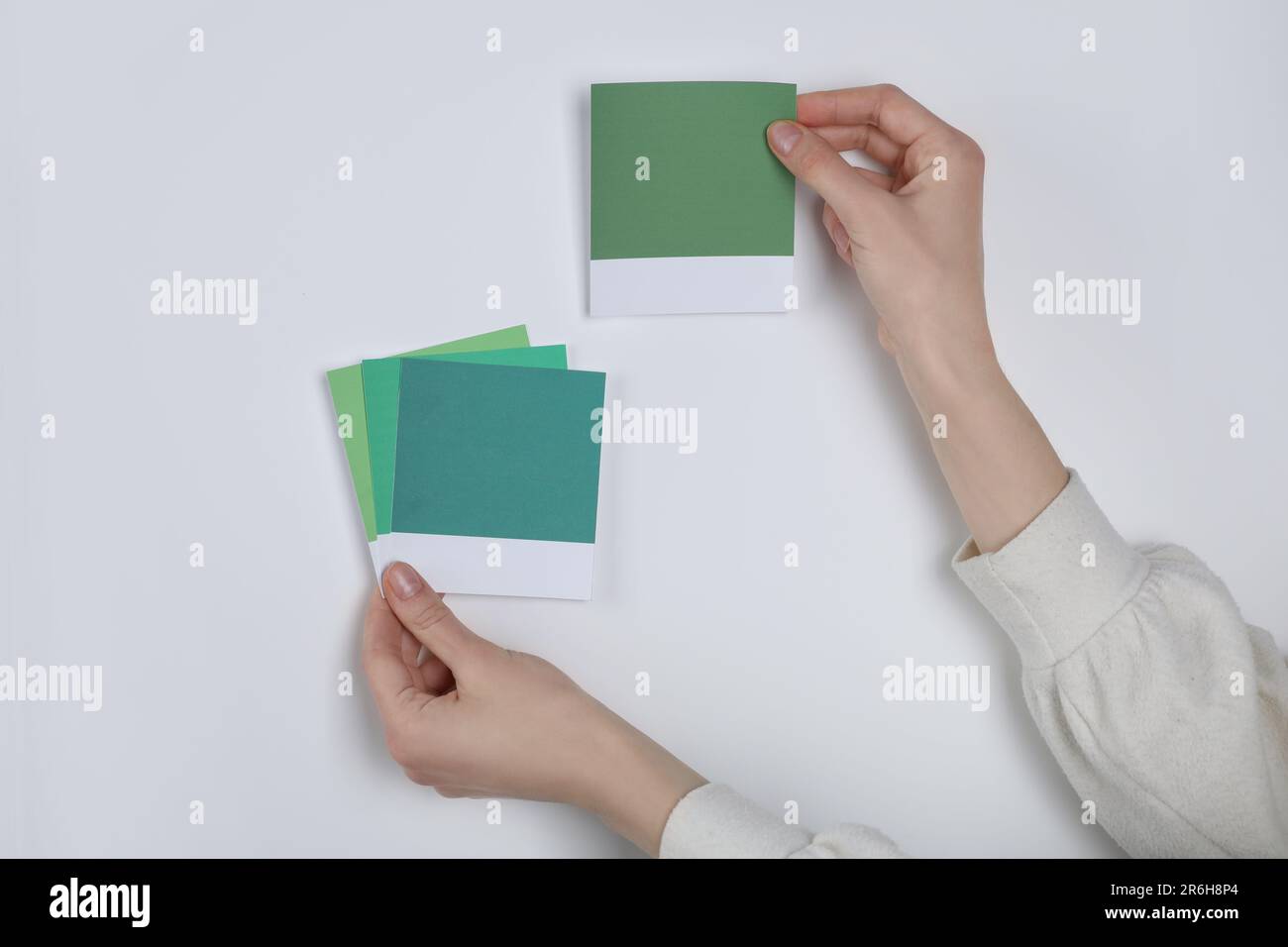 Woman with color sample cards choosing paint shade near white wall ...