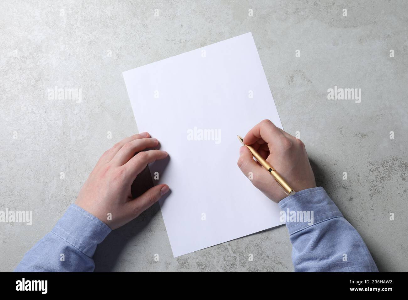 Man writing on sheet of paper with pen at light grey table, top view ...