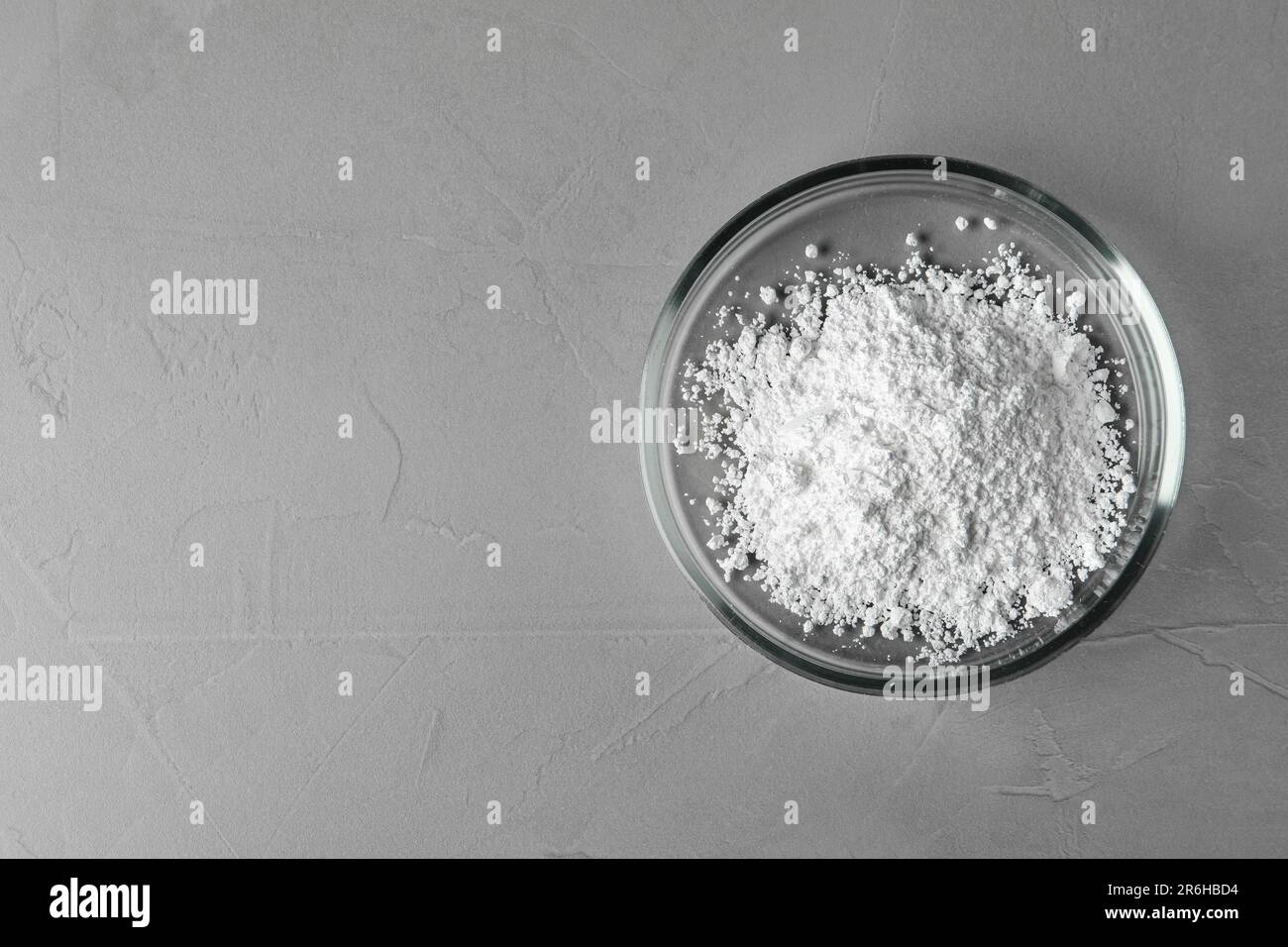 Petri dish with calcium carbonate powder on grey table, top view. Space ...
