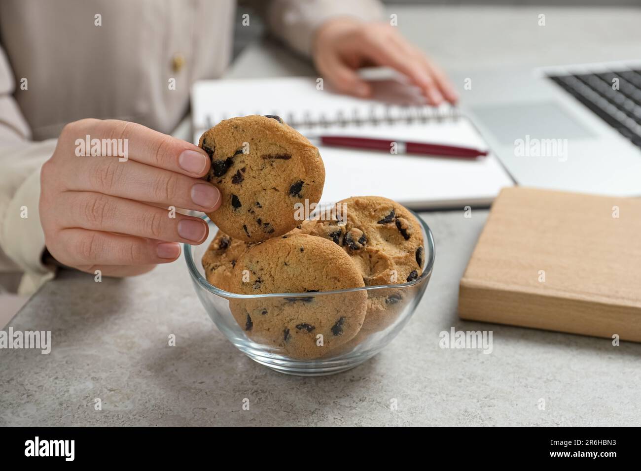Office worker taking chocolate chip cookie from bowl at light gray ...