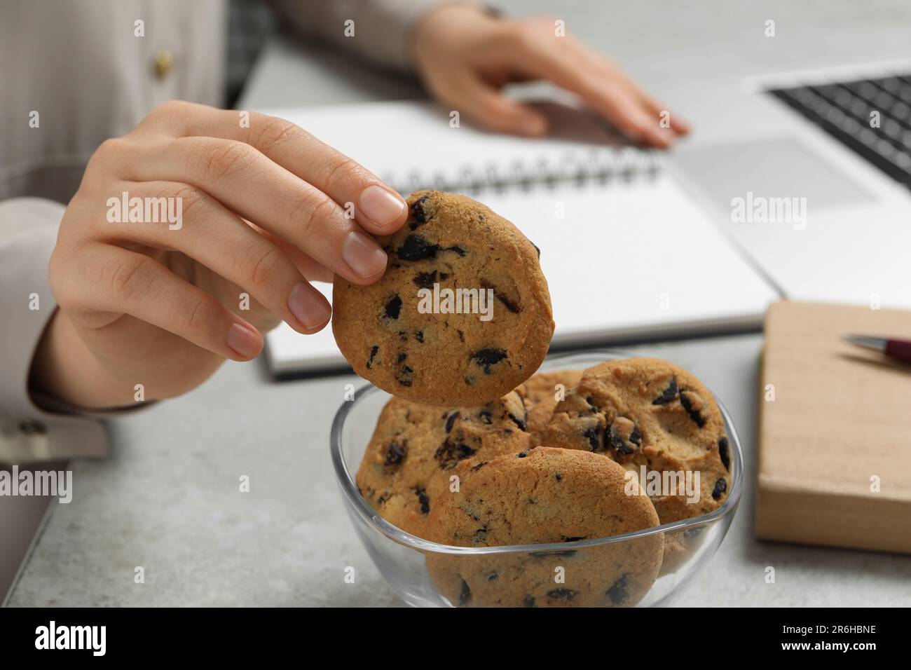 Office worker taking chocolate chip cookie from bowl at light gray ...