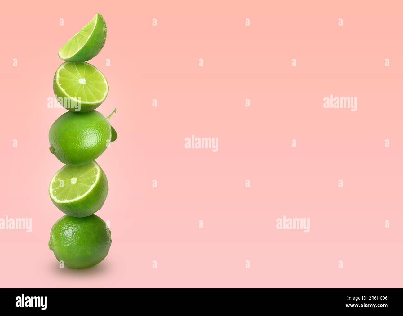 Stacked whole and cut limes on light pink background, space for text ...