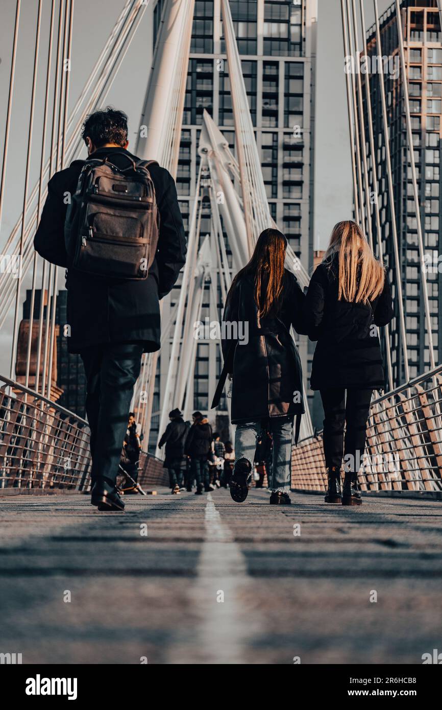 people walking across a pedestrian bridge, with a city skyline ...