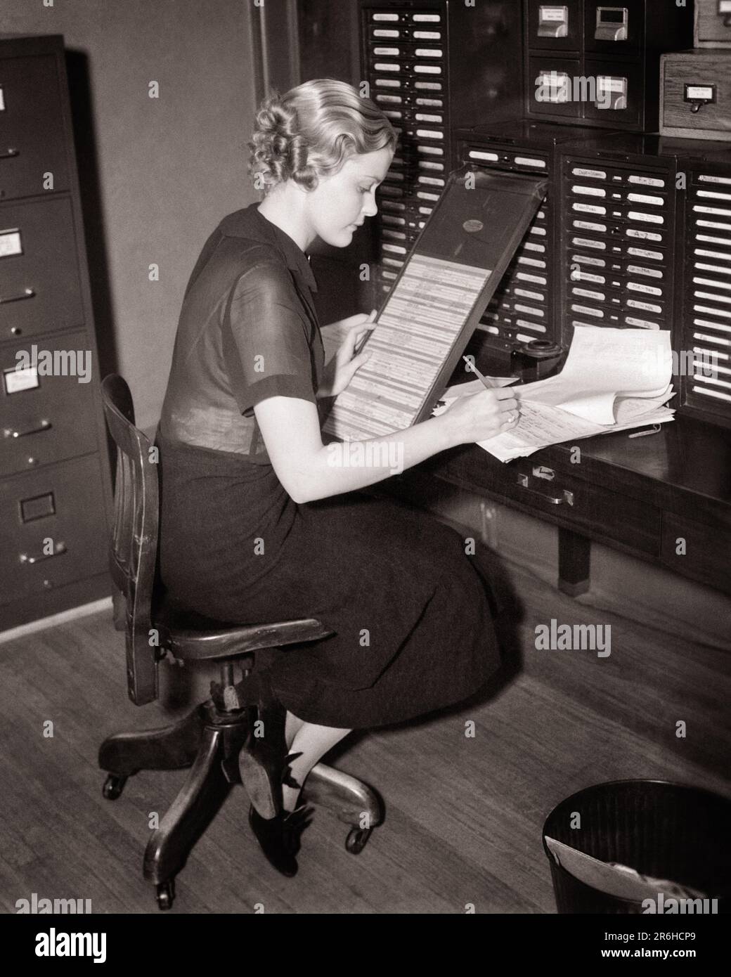 1930s BLONDE YOUNG WOMAN SITTING IN OFFICE CHAIR ENTERING INFO DATA ...