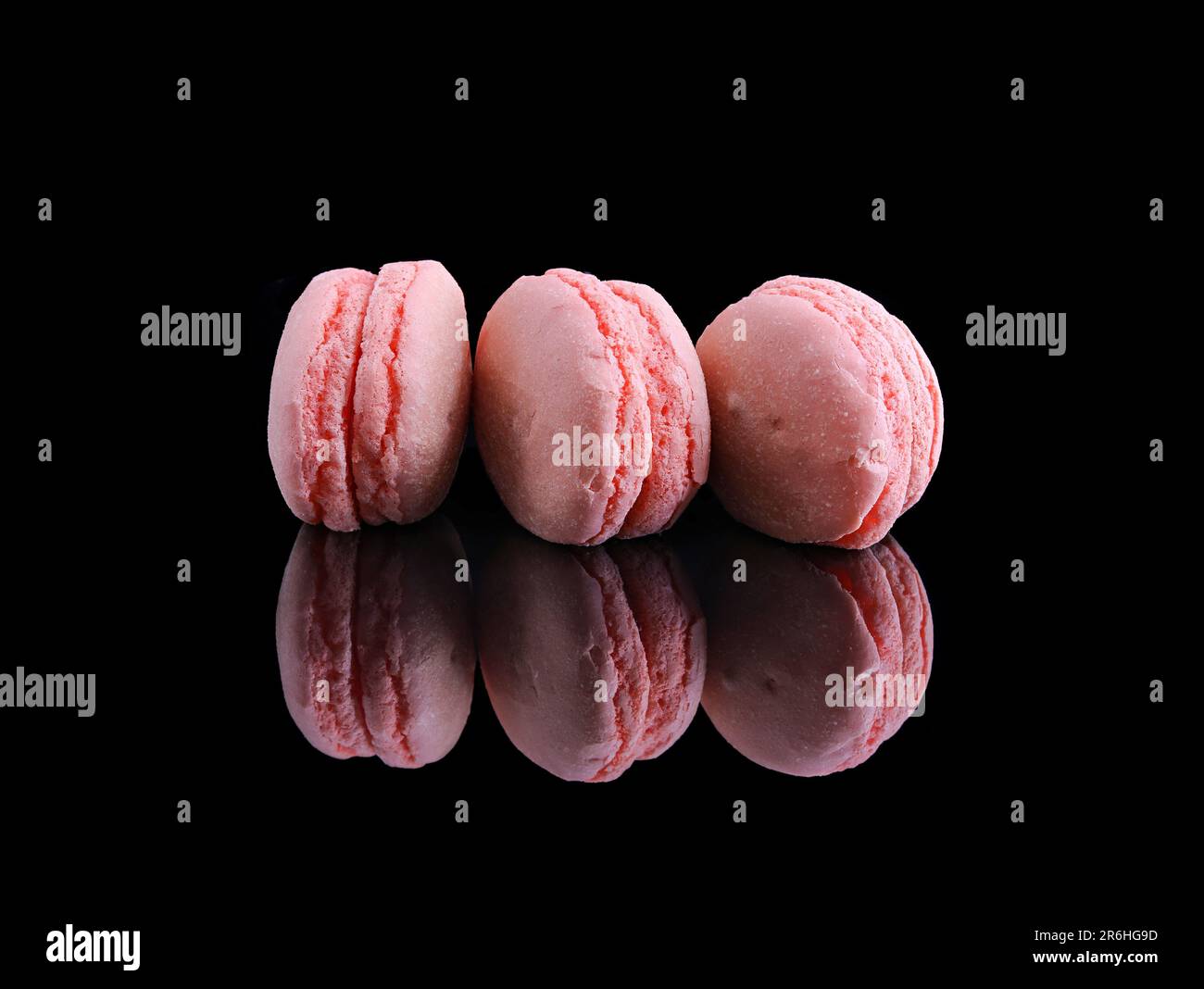 Three colorful macarons lay atop a glossy black surface, with the image ...