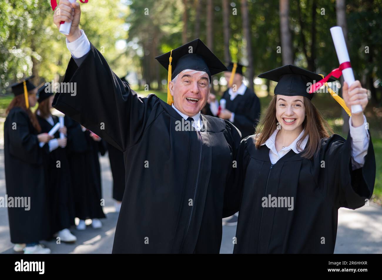 A group of graduates in robes outdoors. An elderly man and a young ...