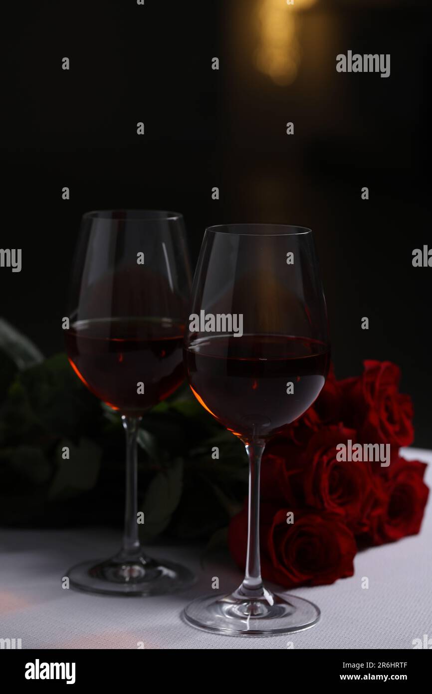 Glasses of red wine and rose flowers on white table. Romantic ...