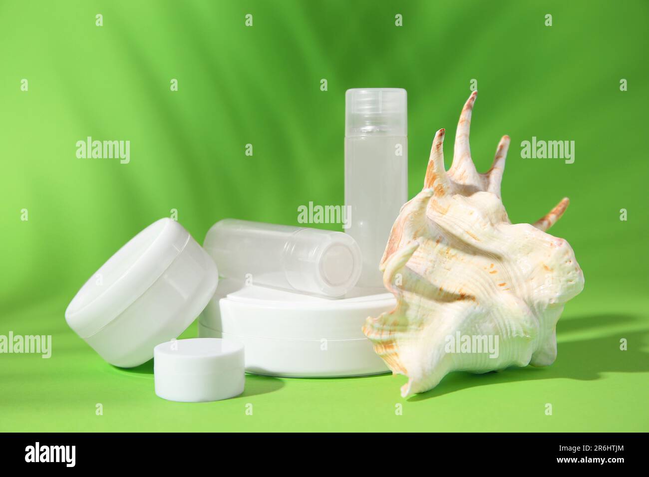 Jars of cream, shampoo samples, lip balm and seashell on light green ...