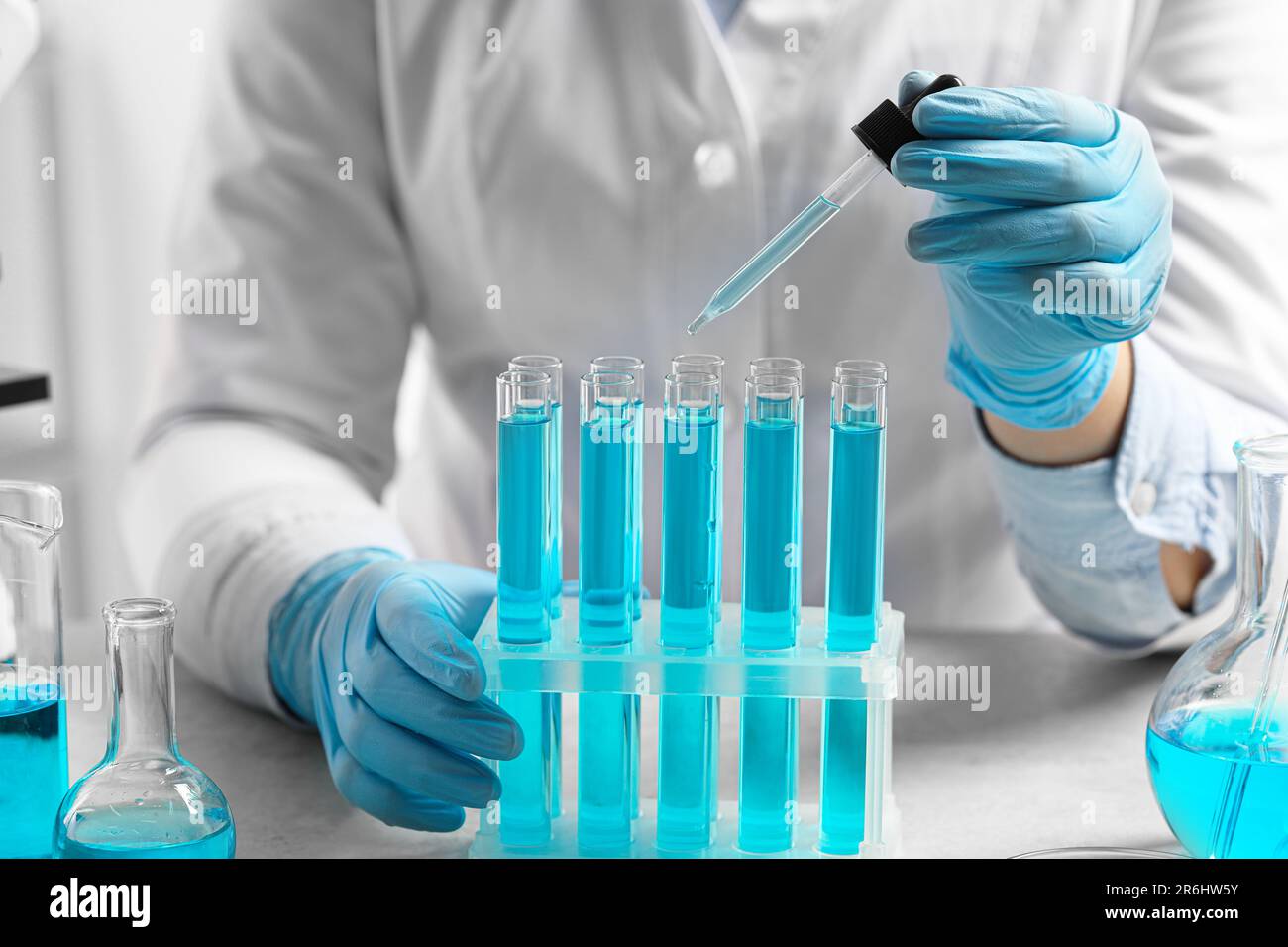 Scientist dripping liquid from pipette into test tube at white table in ...