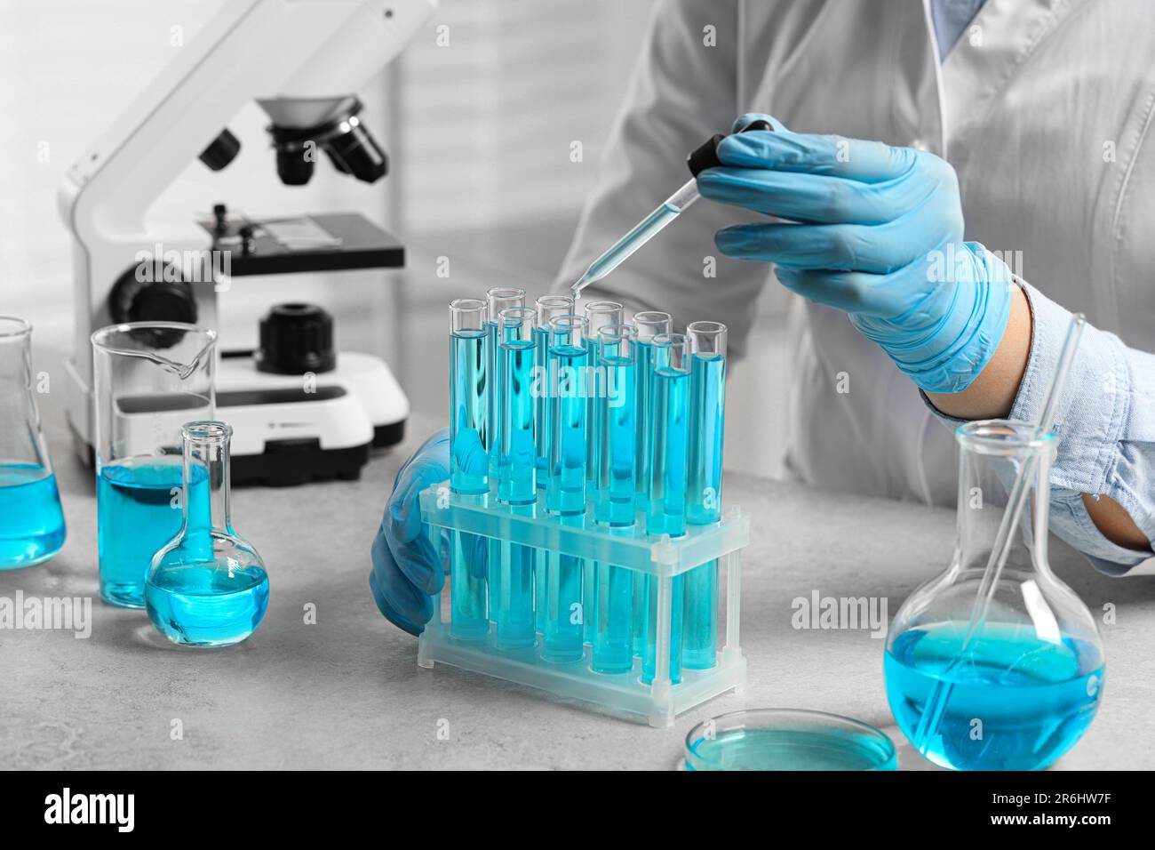 Scientist dripping liquid from pipette into test tube at white table in ...
