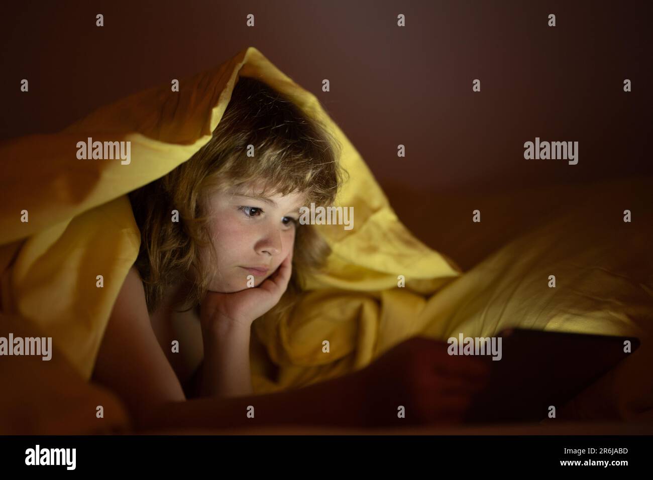 Kid boy lying on bed and surfing Internet on tablet in dark room. Child ...
