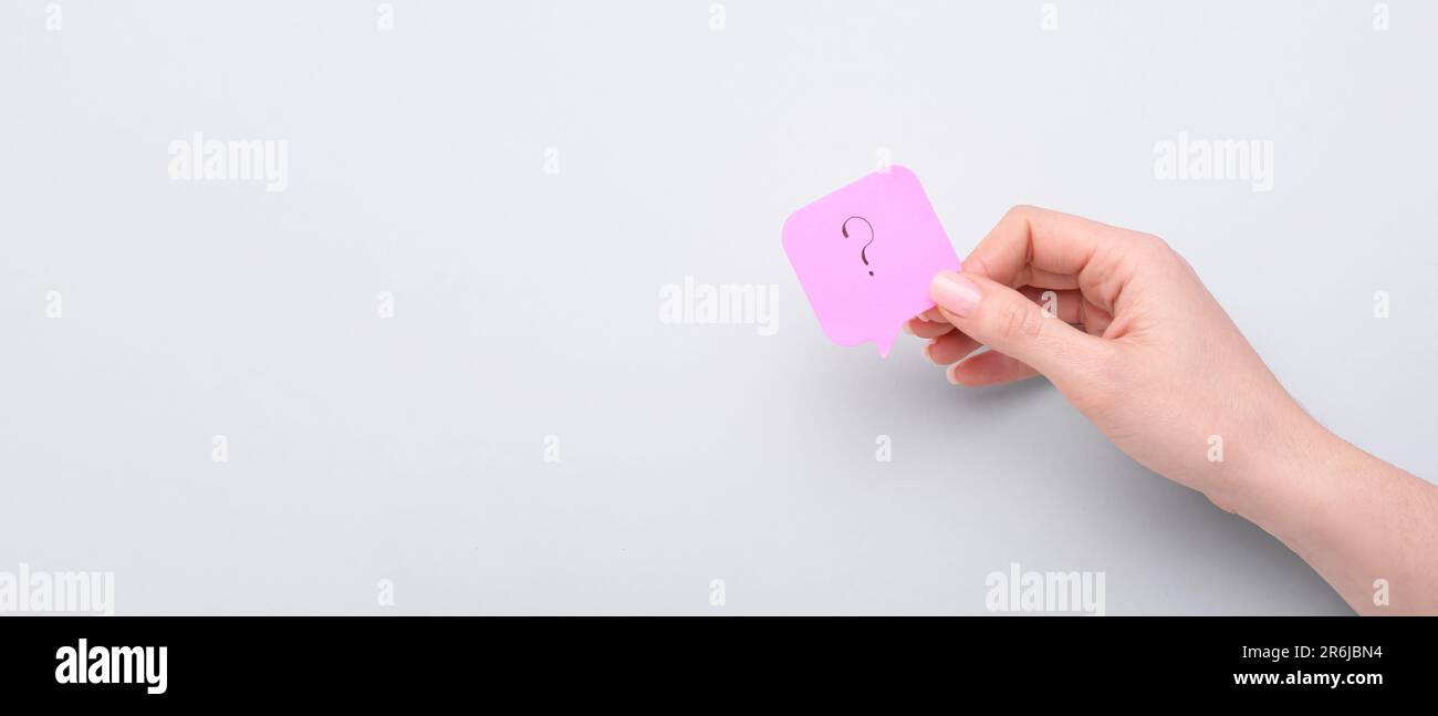Female hand holding sticky paper with question mark on light background ...