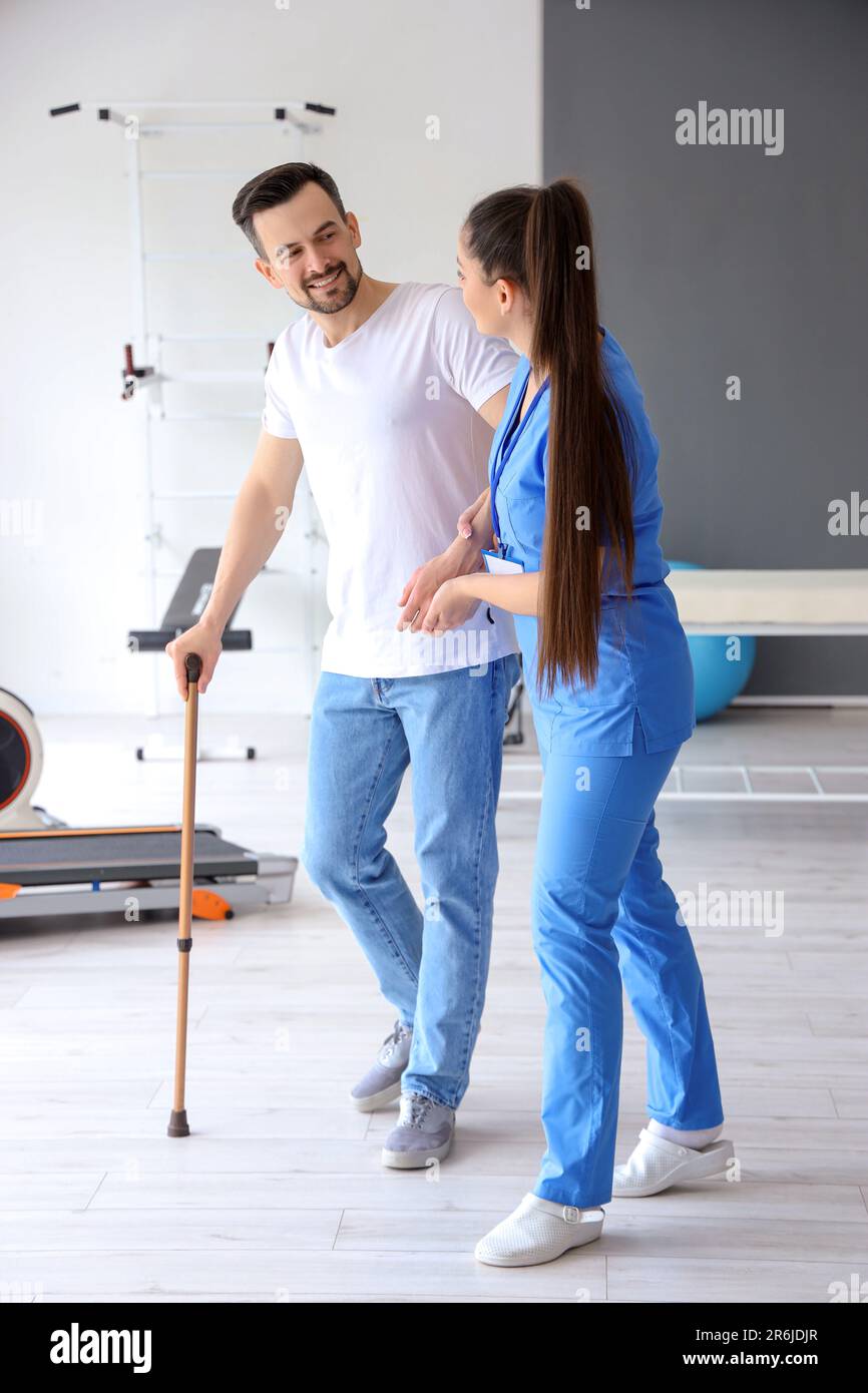Female physiotherapist helping young man with walking stick in ...