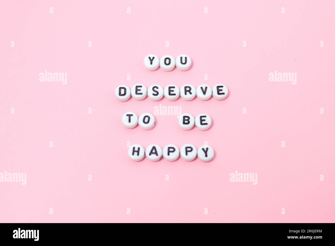 Top view of "you deserve to be happy" quotes made out of beads on pink ...
