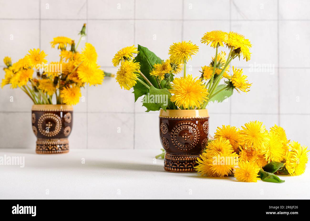 Vases with beautiful dandelion flowers on table near light tile wall ...