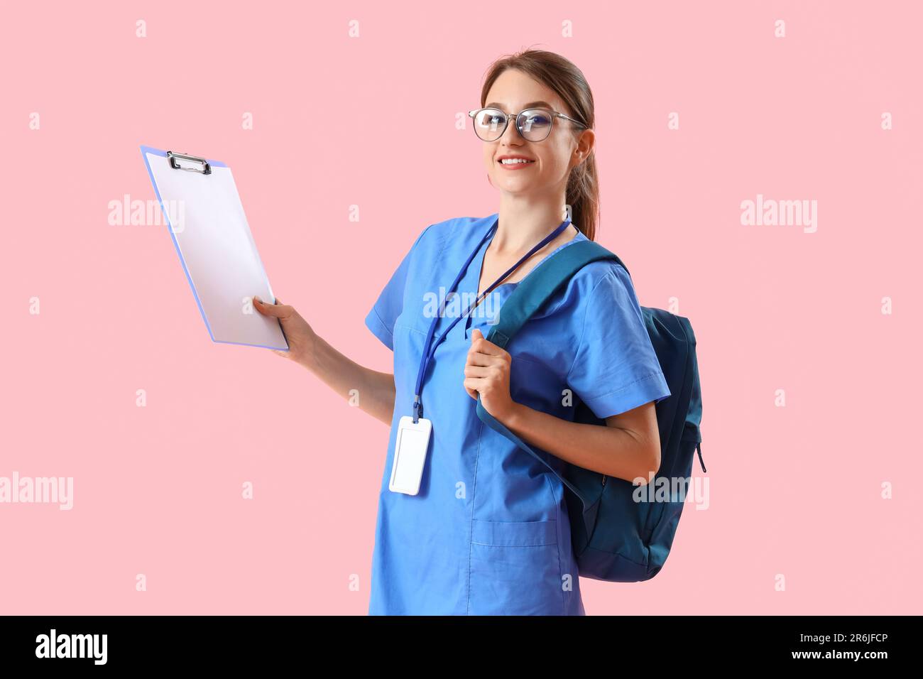 Female medical intern with clipboard and backpack on pink background ...