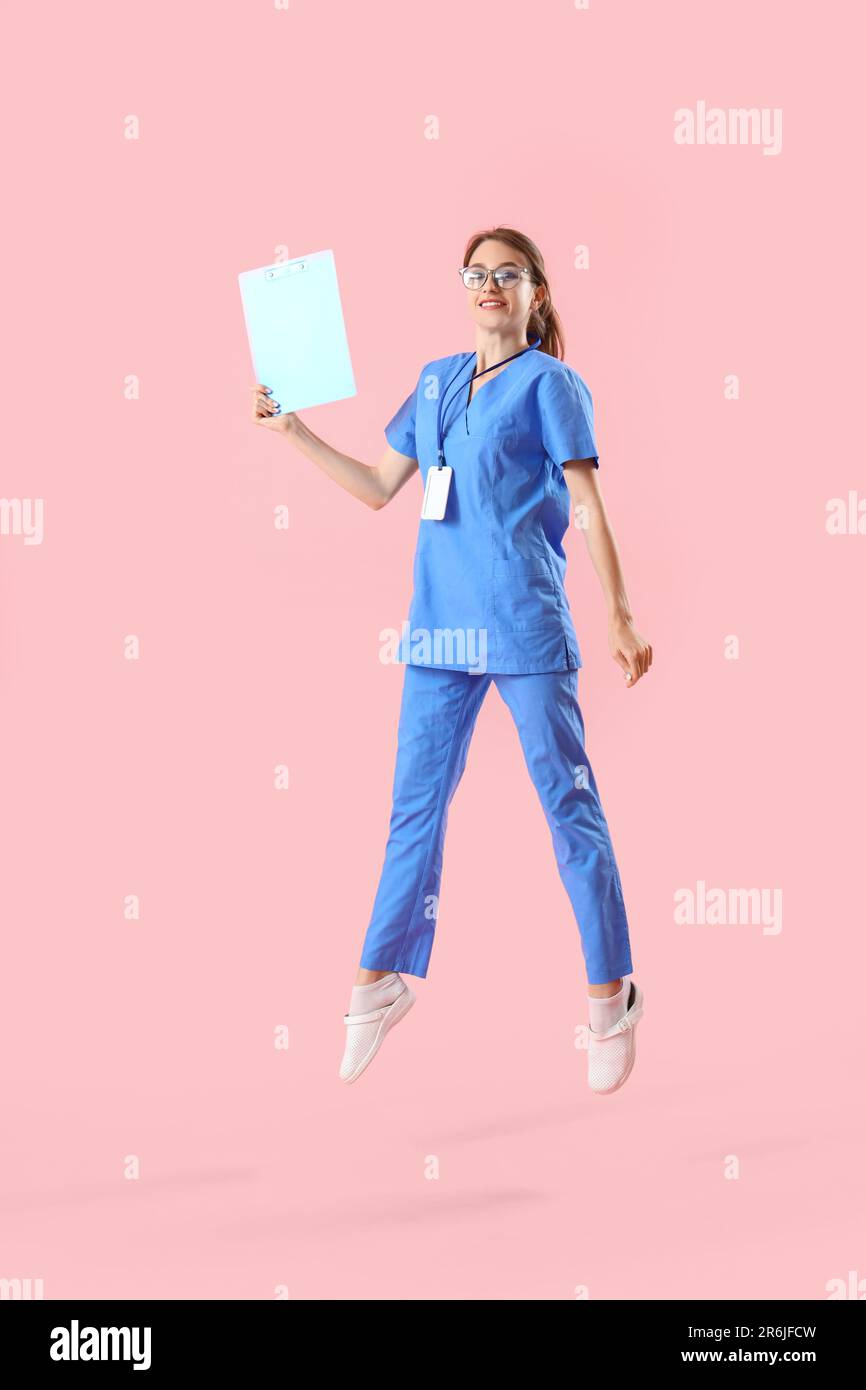 Female medical intern with clipboard jumping on pink background Stock ...