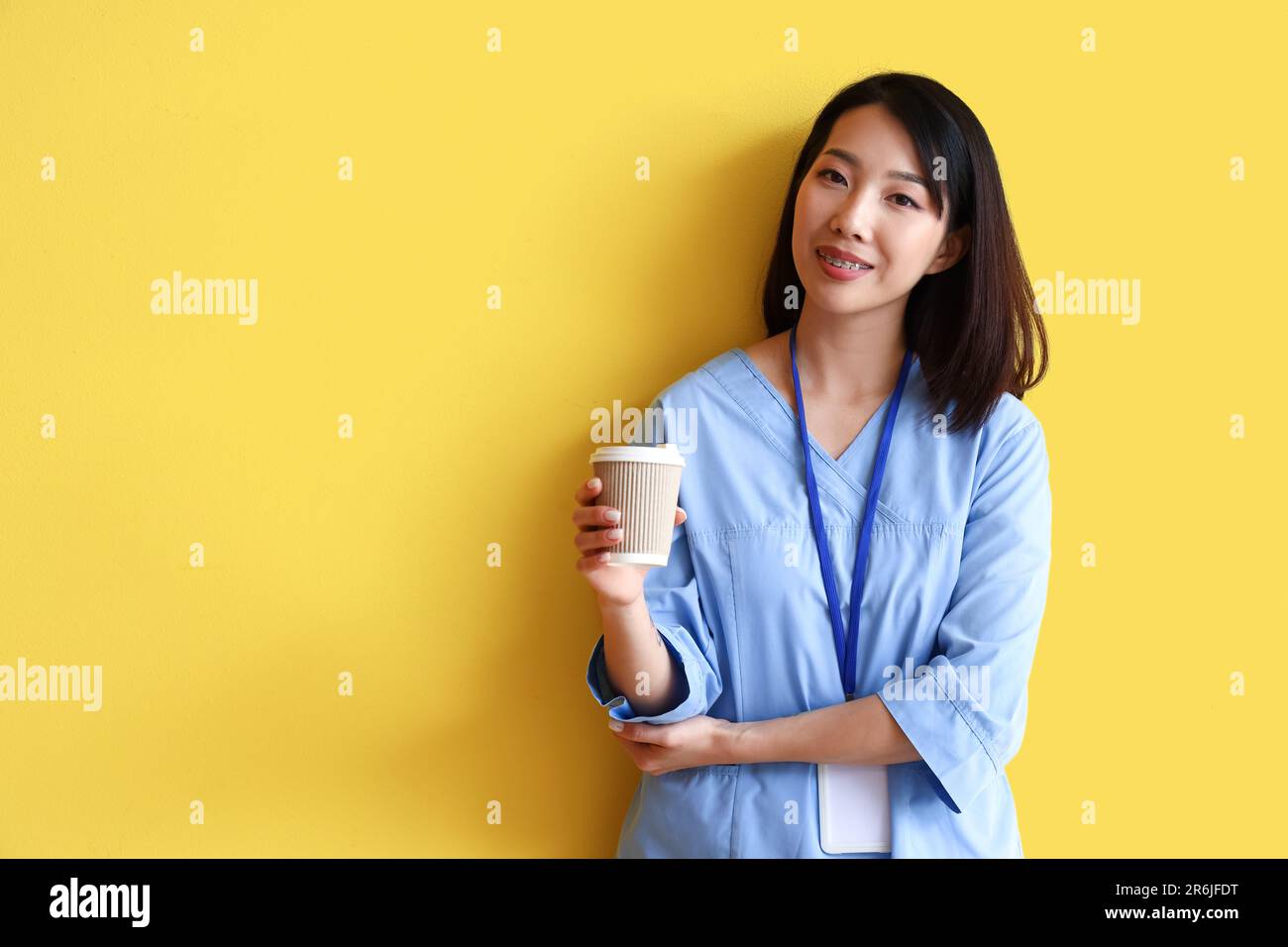 Female Asian medical intern with cup of coffee on yellow background ...