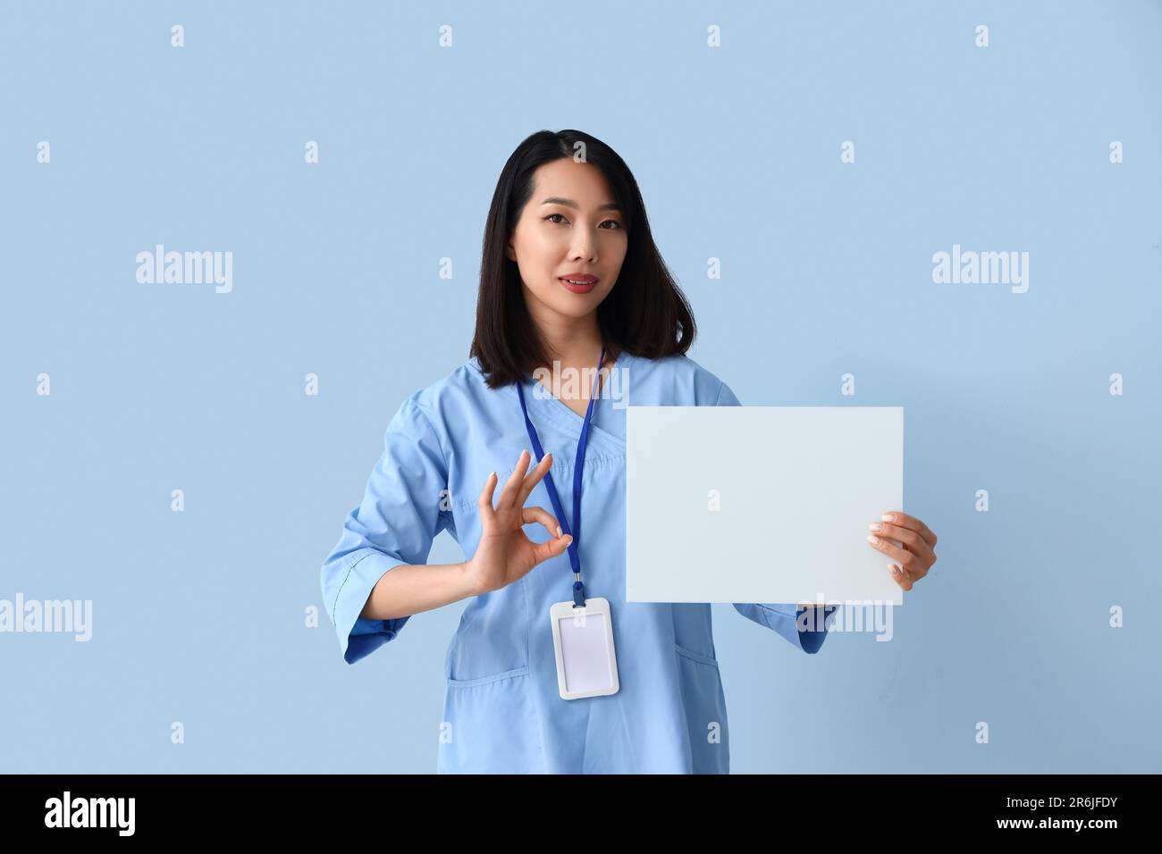 Female Asian medical intern with blank paper sheet on blue background ...