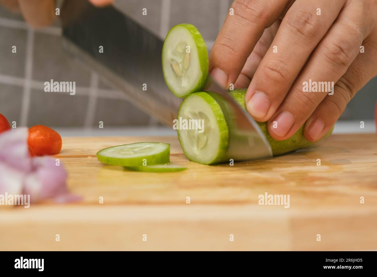 Female hand using a knife to slice cucumbers on a cutting board. Close ...
