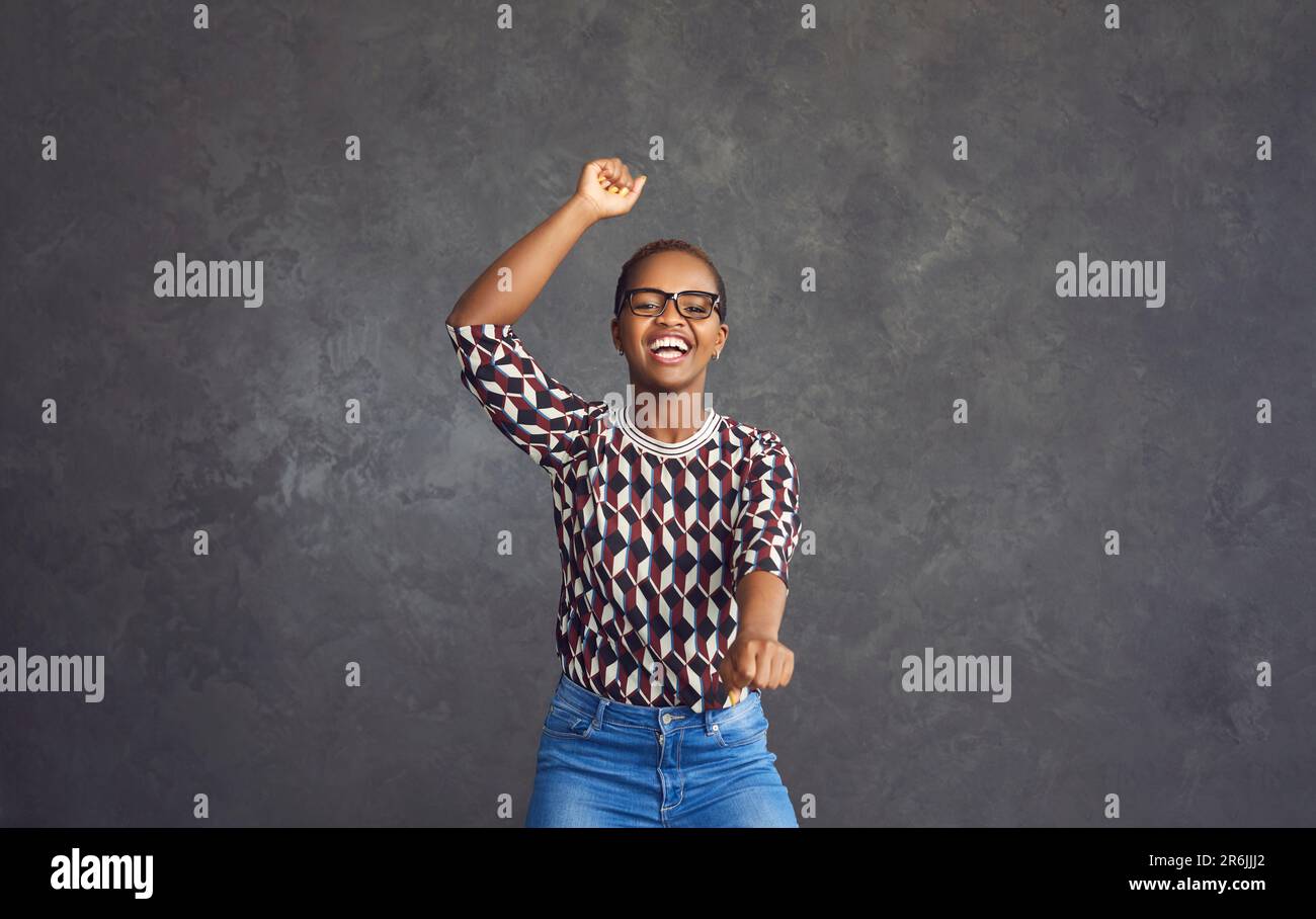Happy excited young black woman dancing gangnam style against grey ...