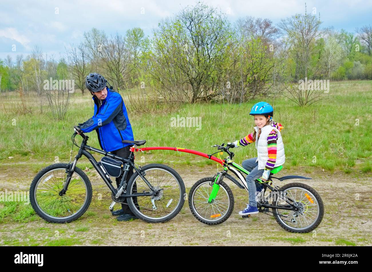 Family cycling, father teaches child to ride bicycle with bike tow bar ...