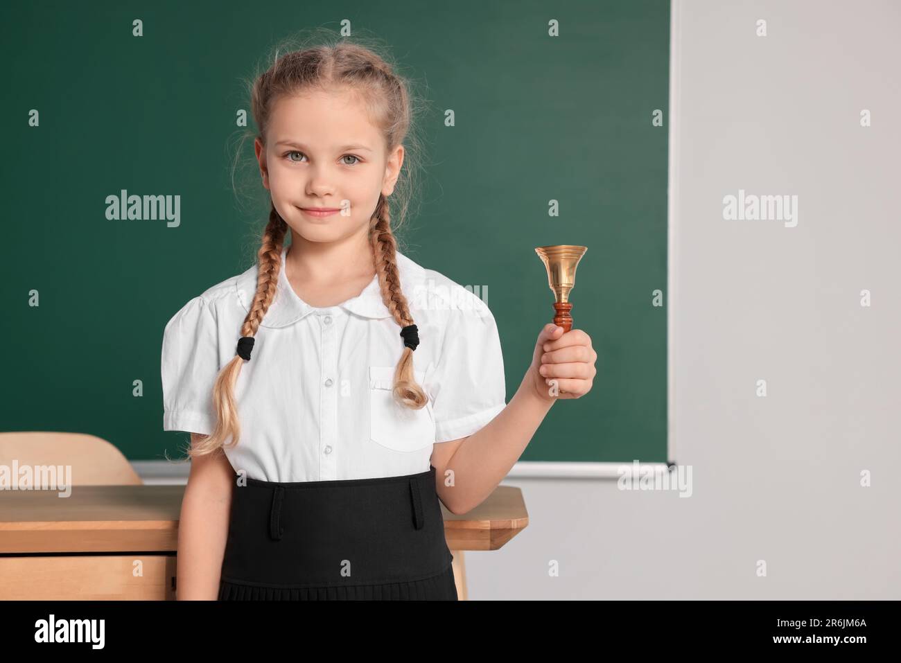 Pupil with school bell near chalkboard in classroom Stock Photo - Alamy