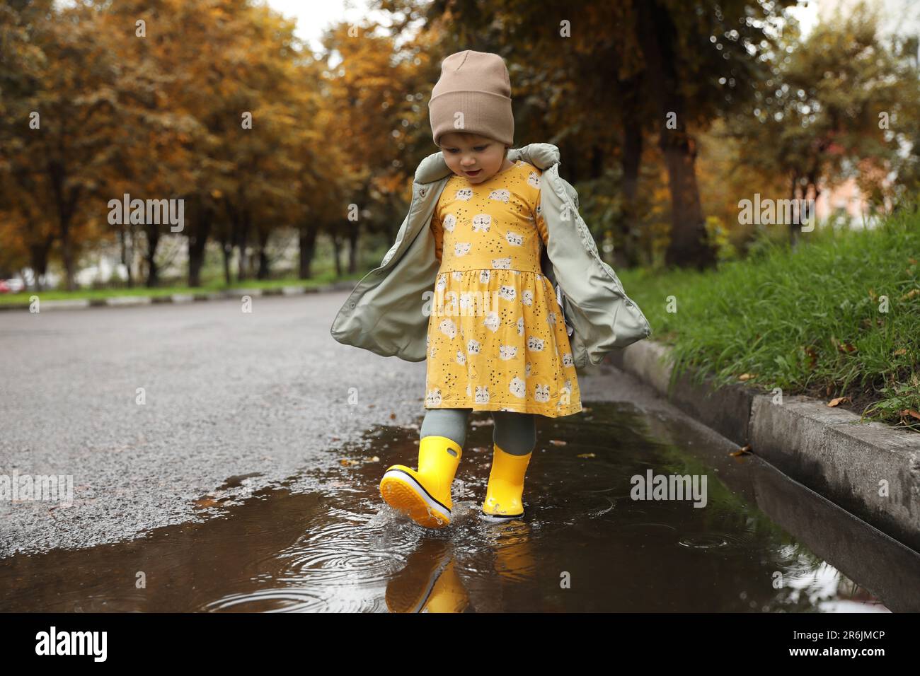 Cute little girl splashing water with her boots in puddle outdoors ...