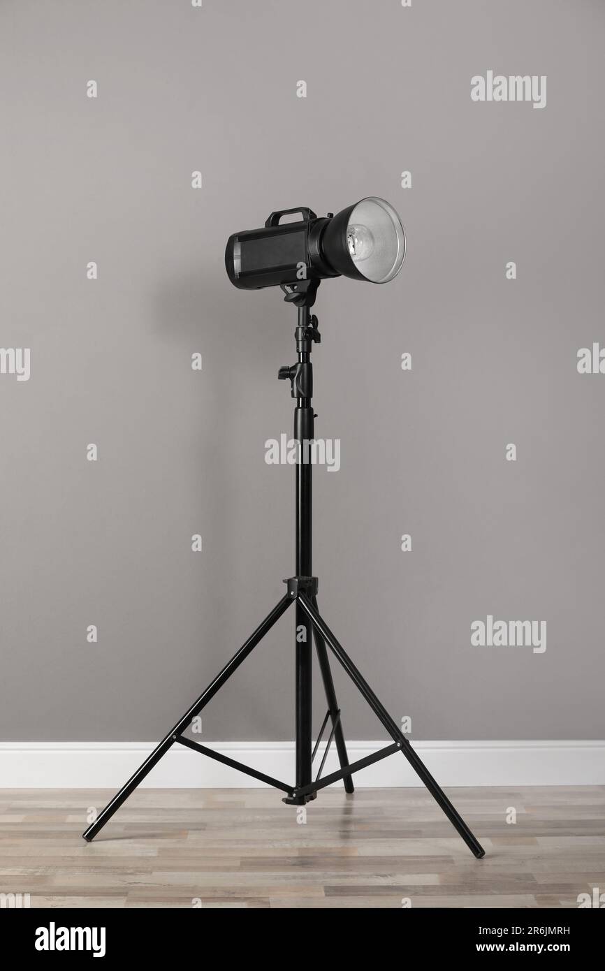 Professional studio flash light with reflector on tripod near grey wall ...
