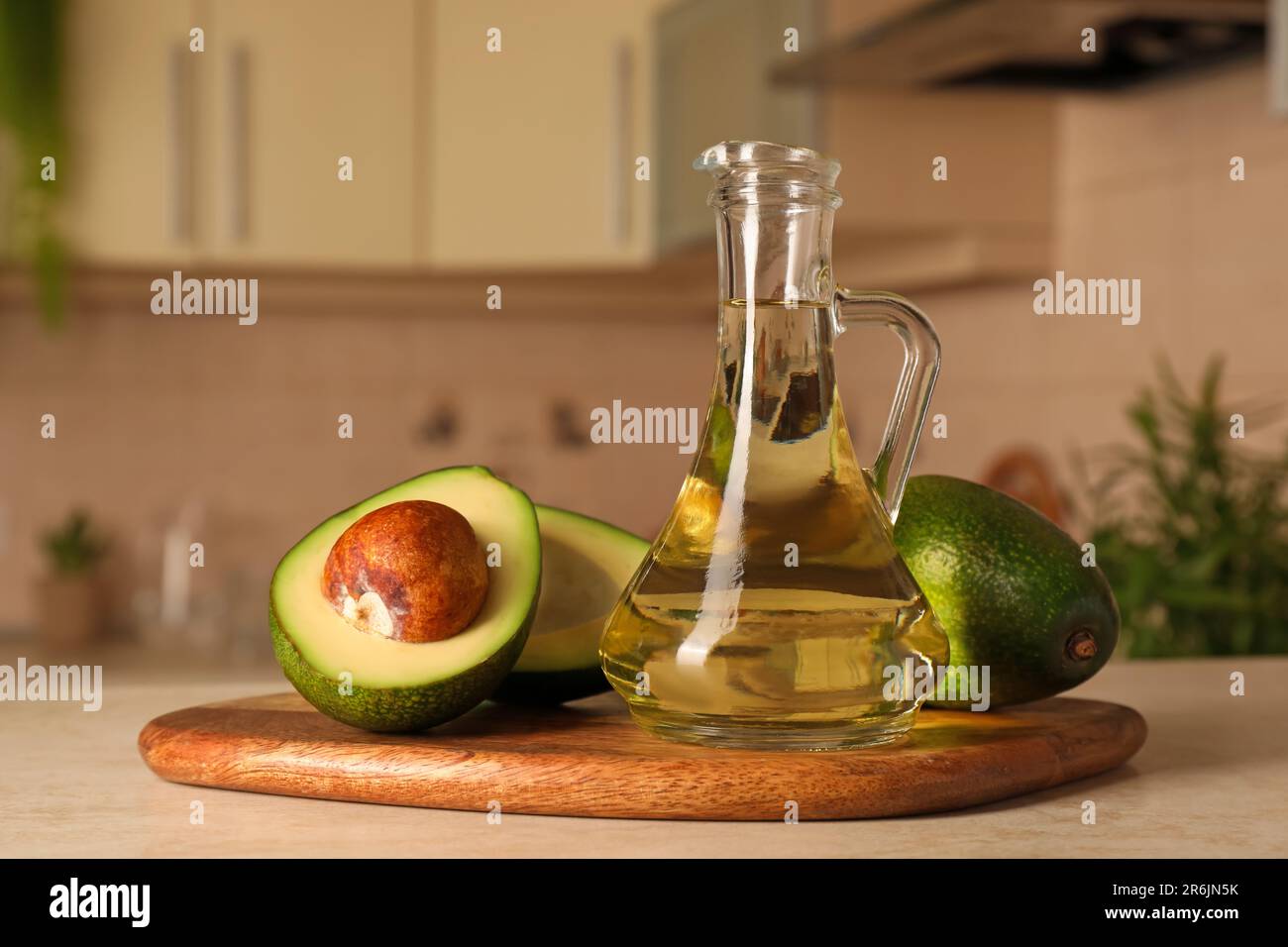 Fresh avocados and jug of cooking oil on beige marble table in kitchen ...