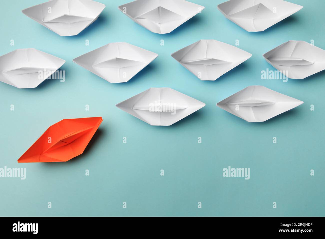 Orange paper boat floating away from others on light background, flat ...