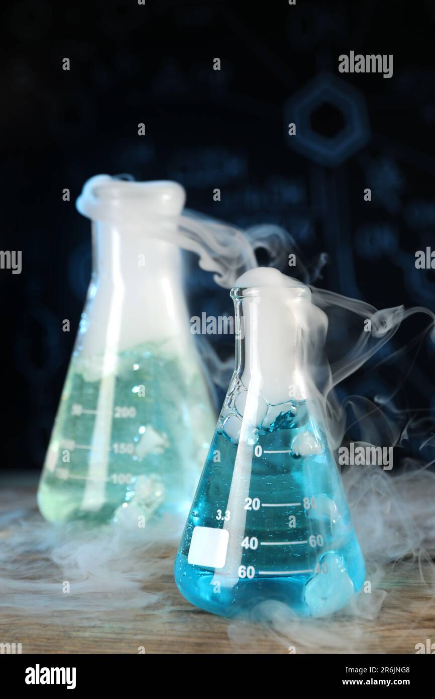 Laboratory glassware with colorful liquids and steam on wooden table ...