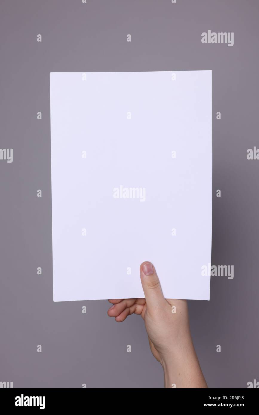 Woman holding sheet of paper on grey background, closeup. Mockup for ...