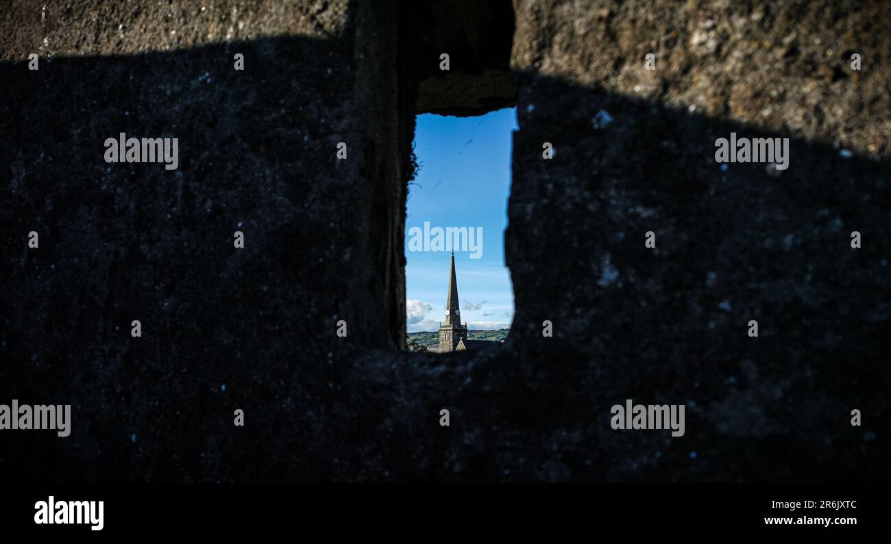 An imposing grand church through a hole in a weathered stone wall ...