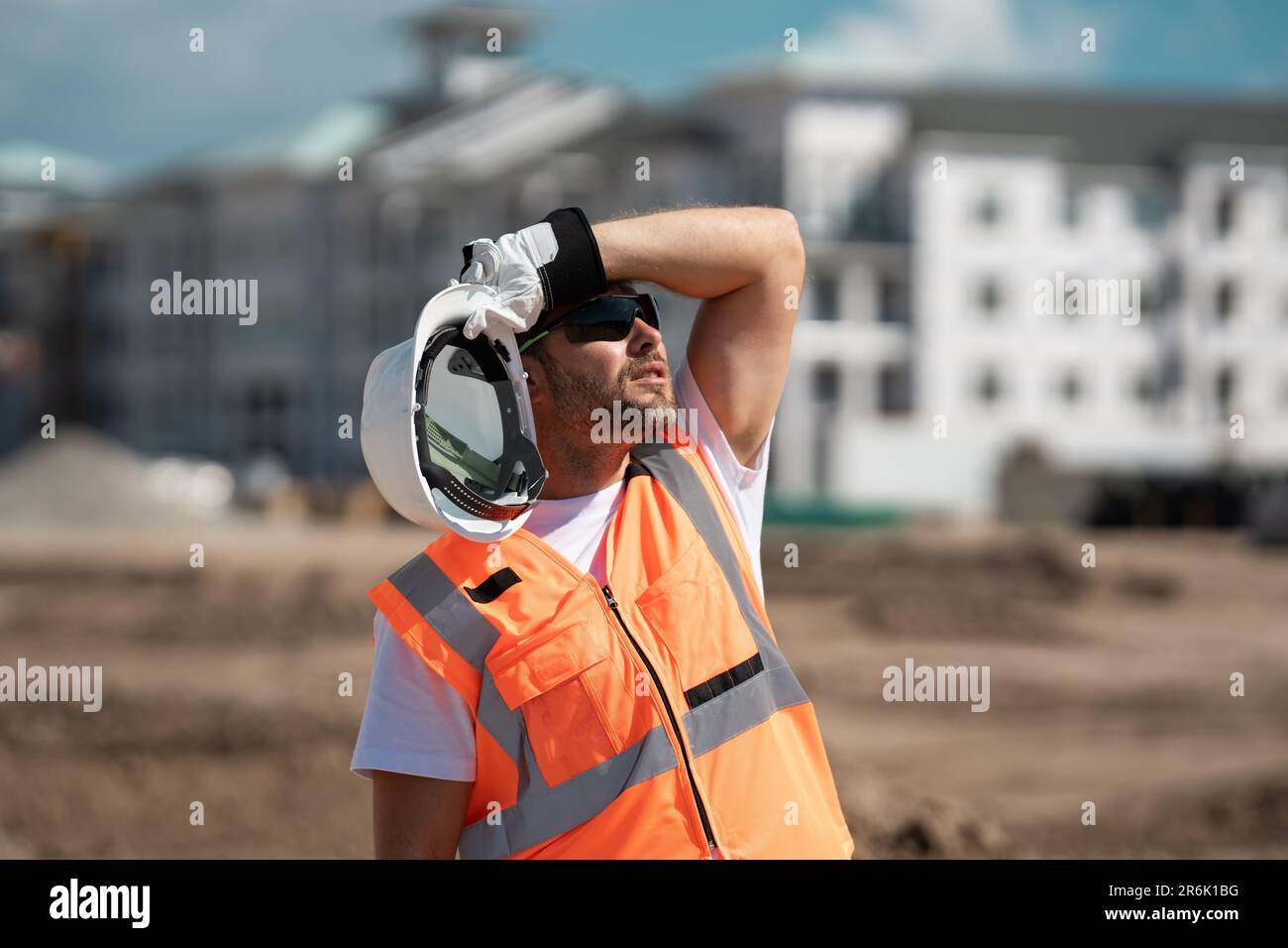 Tired worker. Construction site worker in helmet working outdoor. A builder in a safety hard hat ...