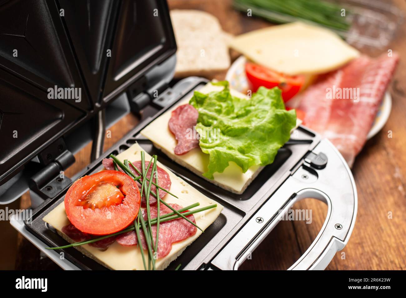 A sandwich maker with two different sandwiches with tomatoes, ham ...