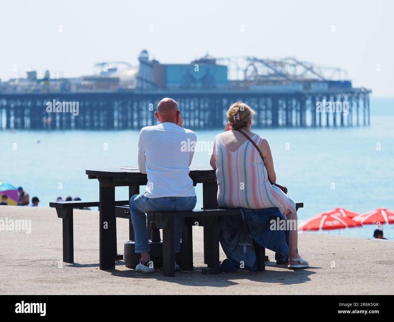 A couple sit on a bench on the seafront at Brighton beach in East ...