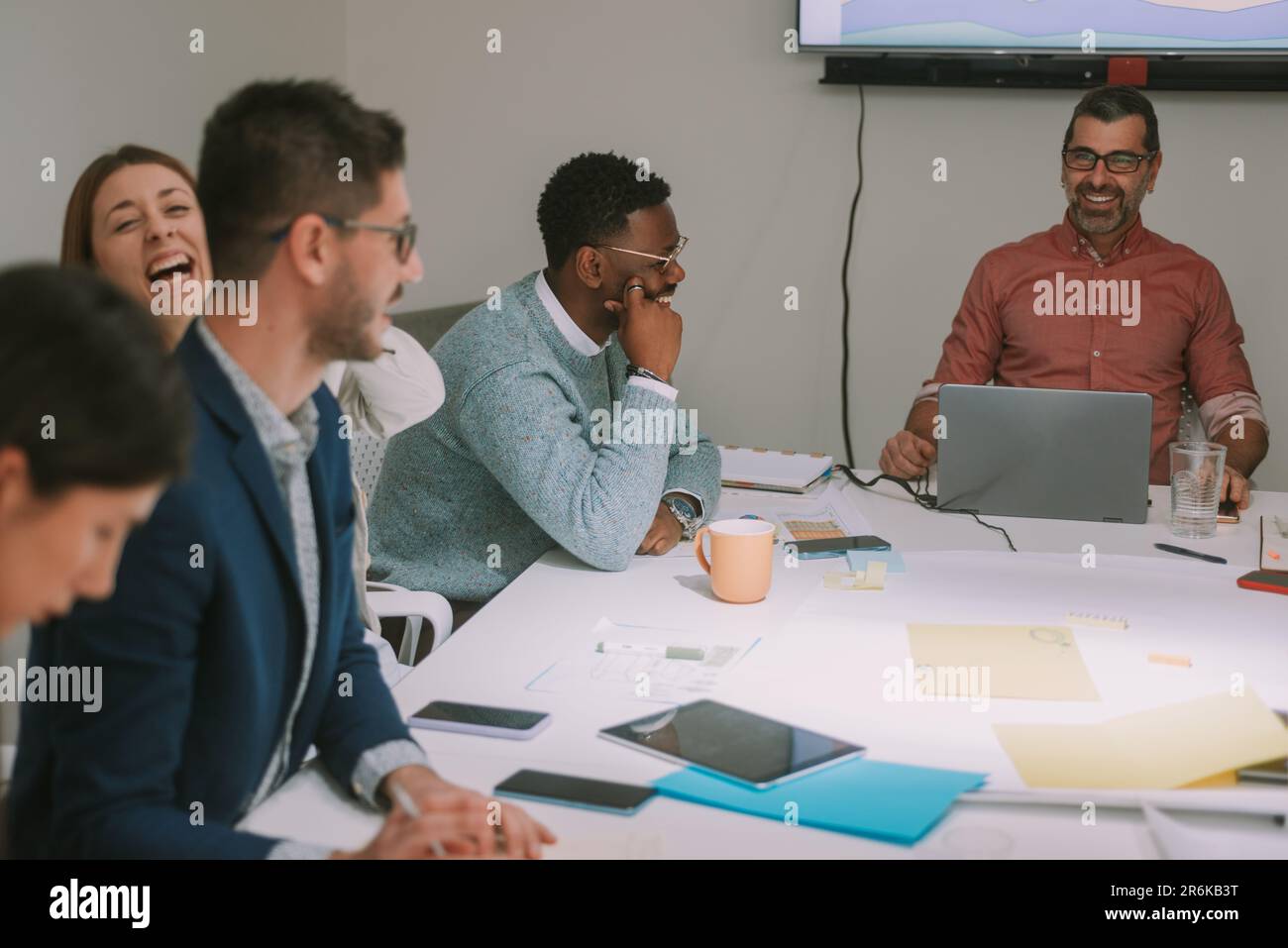 Business colleagues laughing together while sitting at the office desk at the co working space ...