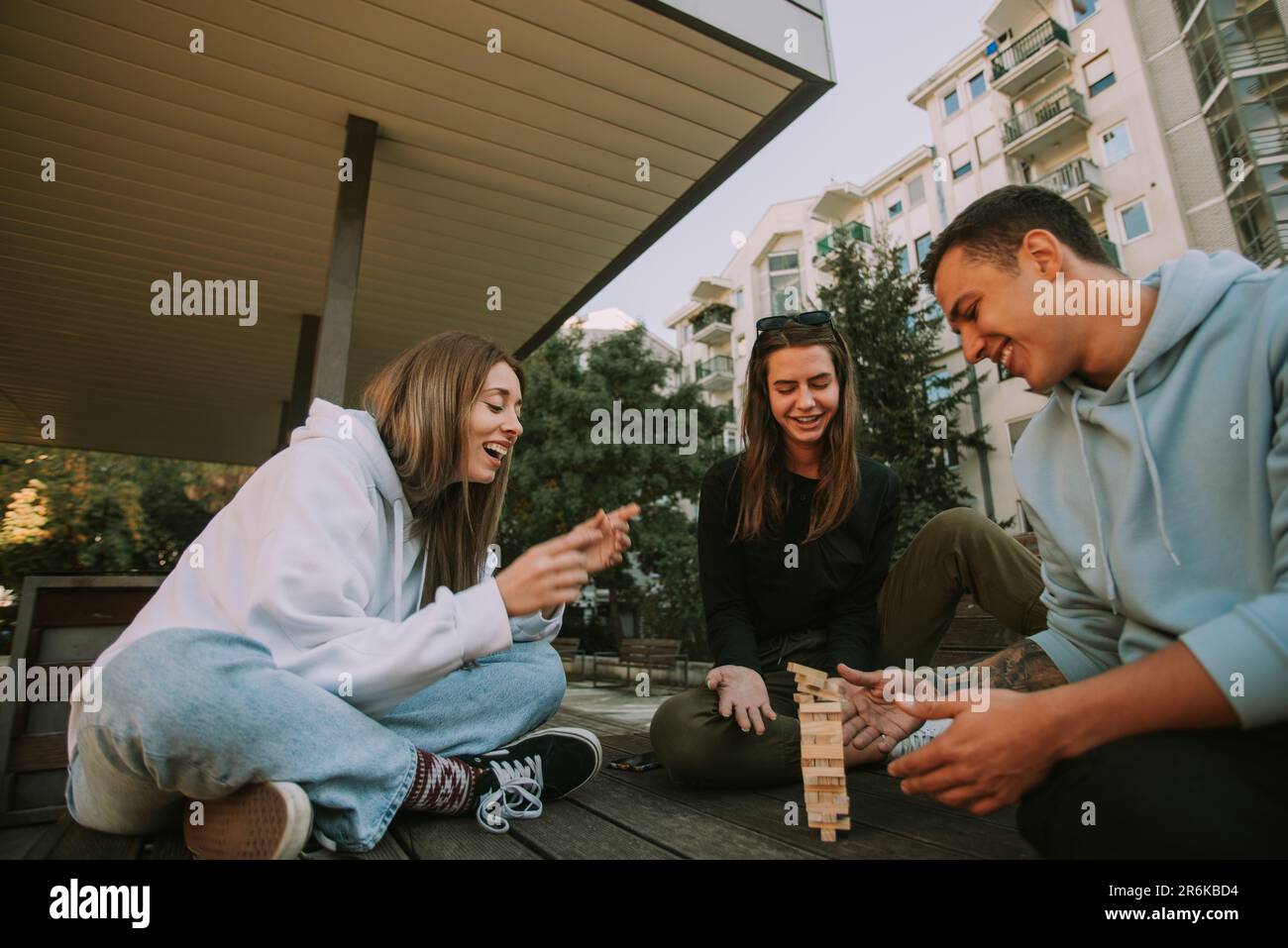 Three best friends smiling while playing jenga on the wooden bench ...