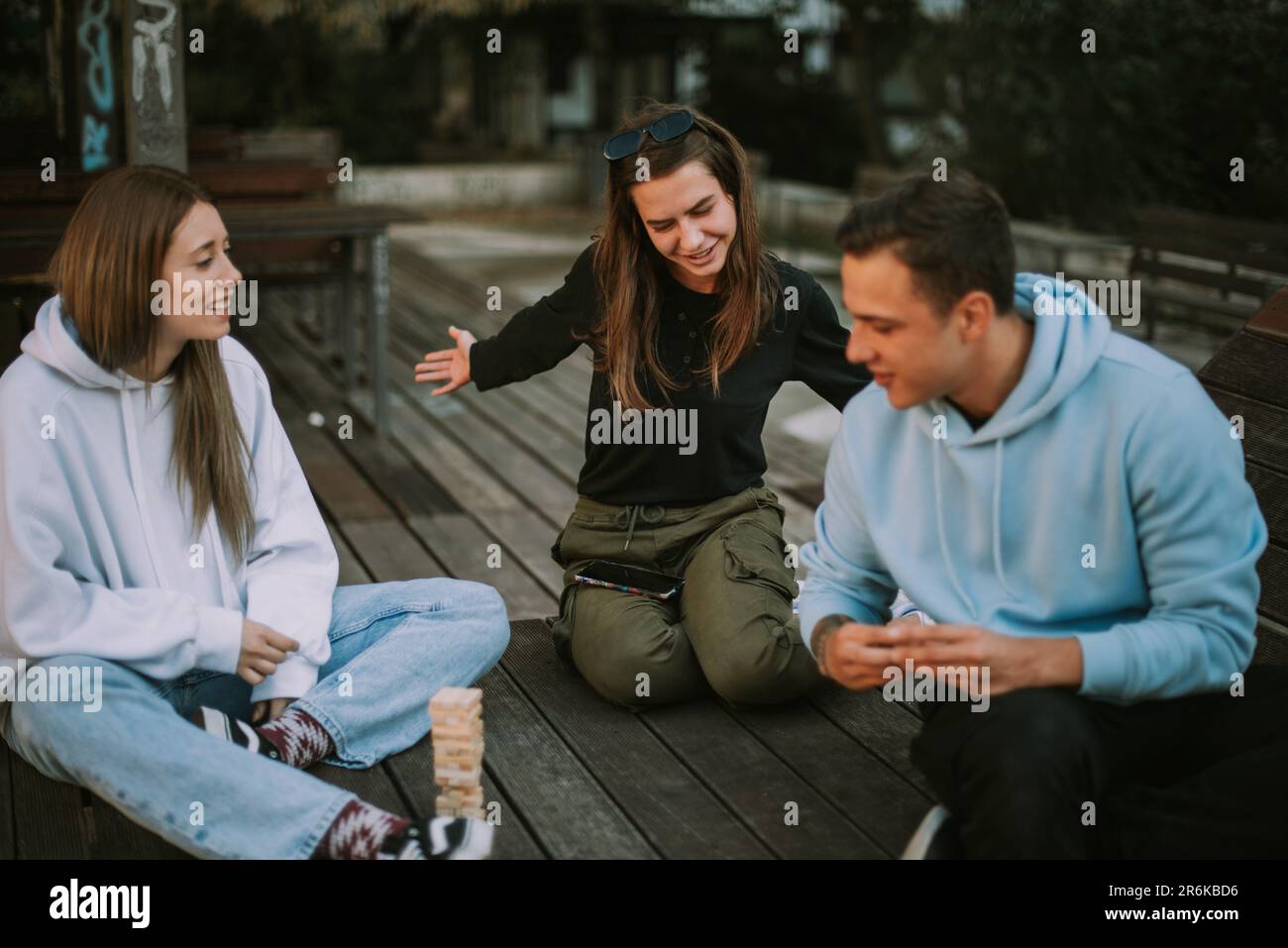 Three friends smiling while playing jenga on the wooden bench Stock ...