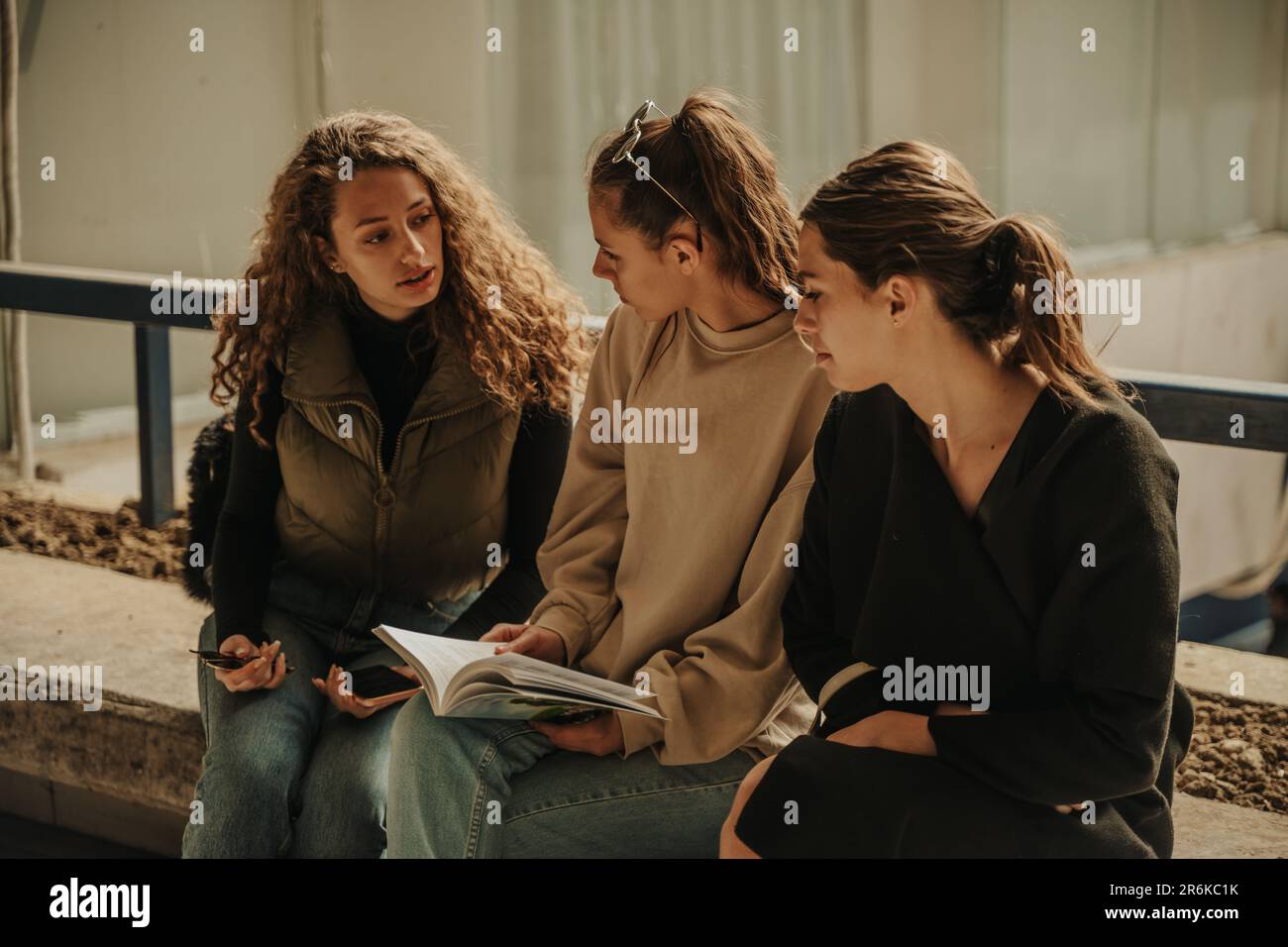 Three girls reading a book together while sitting on a wall. Curly ...