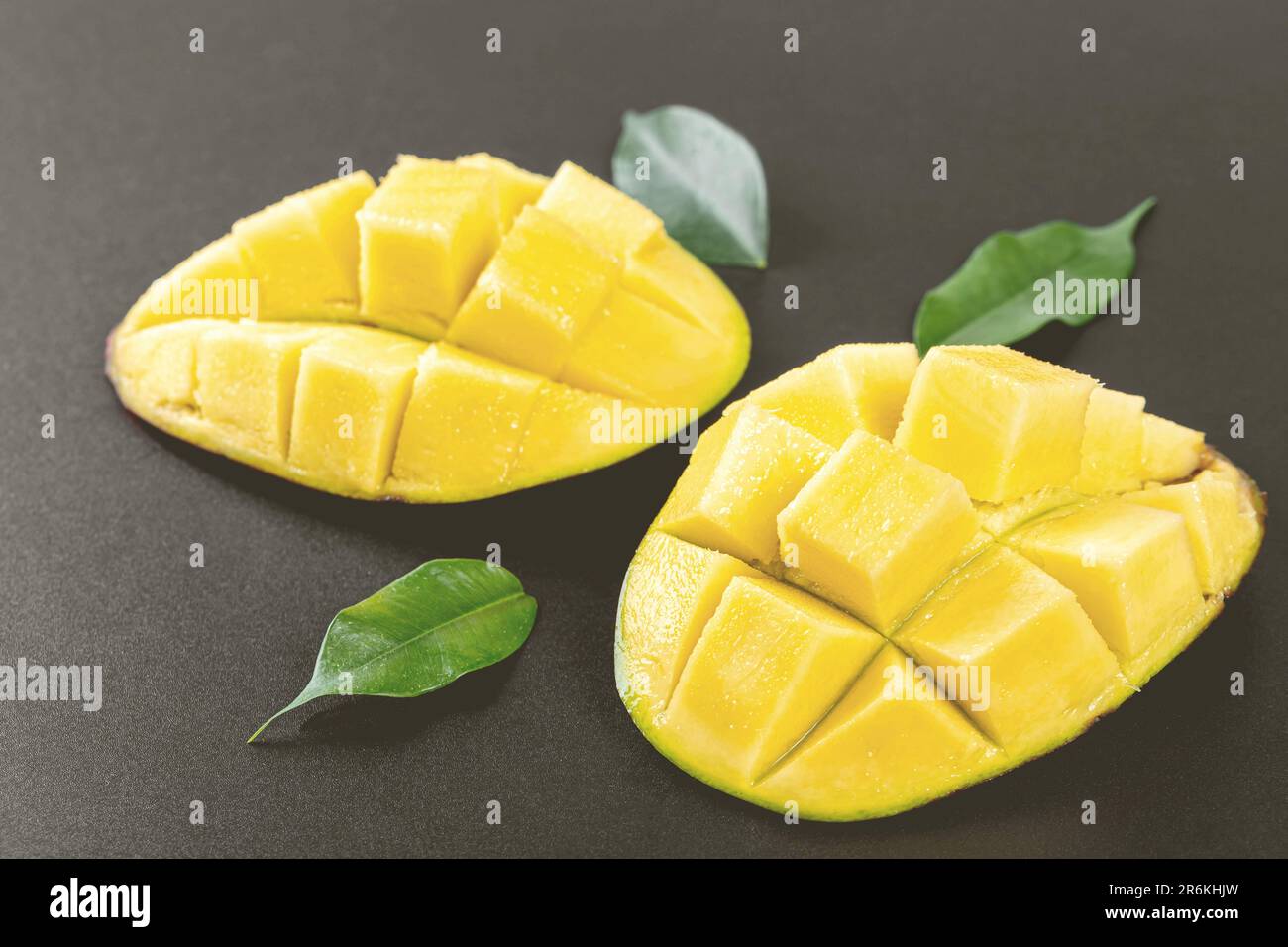 Two ripe yellow mangos cut in half and arranged on a black surface ...